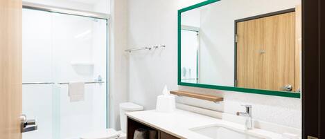 Um banheiro moderno com box de vidro, vaso sanitário branco, toucador de madeira com pia e um espelho grande com moldura verde.