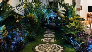 Um corredor com piso estampado, vegetação exuberante e luminárias decorativas.