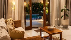 Uma sala de estar moderna com um sofá, mesa de centro e vista para uma piscina através de portas de vidro.