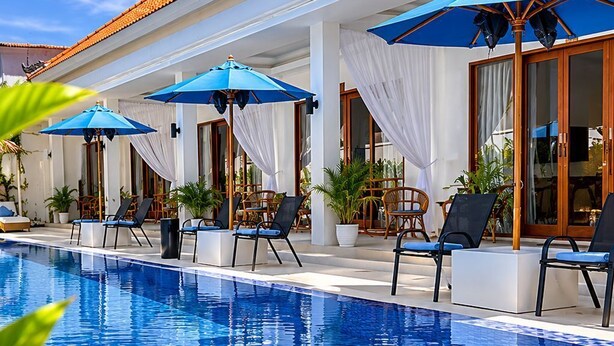 Uma piscina com piso em azulejo, espreguiçadeiras e guarda-sóis.