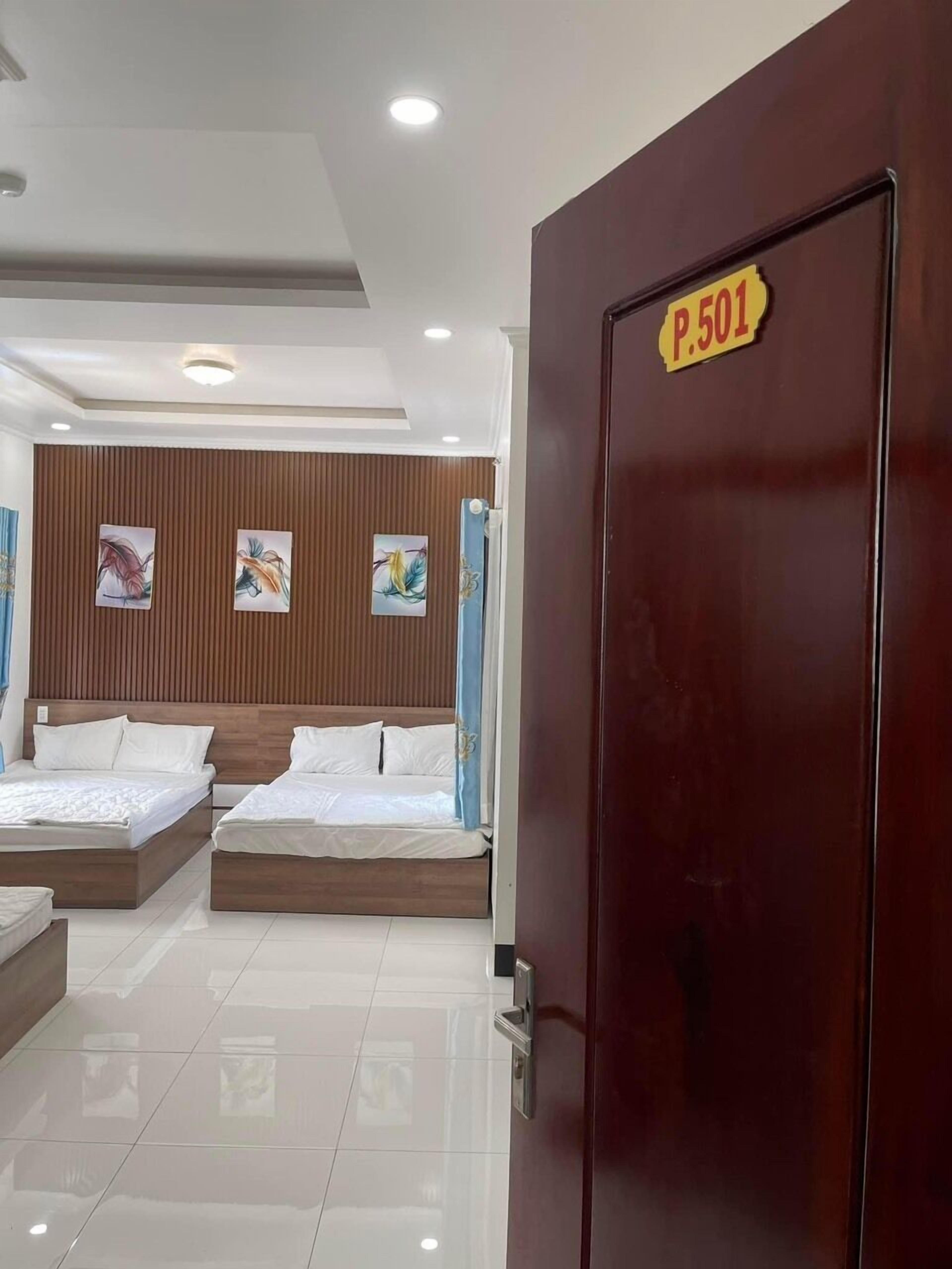 Quarto de hotel com duas camas, lambris de madeira nas paredes e uma porta com a inscrição P.501.