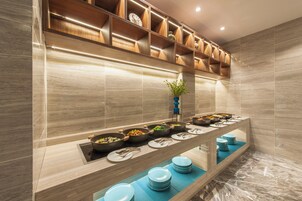 Buffet montado com diversas estações de comida, um relógio e um vaso de planta.