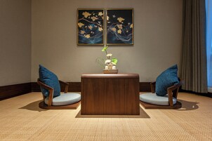 Um quarto com uma mesa redonda de madeira, duas cadeiras com almofadas azuis, um vaso com flores e dois quadros na parede.