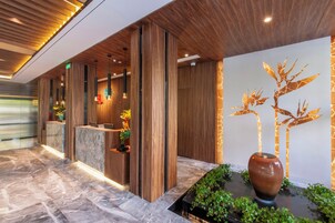 Uma área de recepção moderna com lambris de madeira, piso de mármore e um vaso decorativo com plantas.