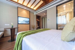 Quarto de hotel com uma cama, uma mesinha com um vaso, televisão fixada na parede e um guarda-roupa com porta deslizante.