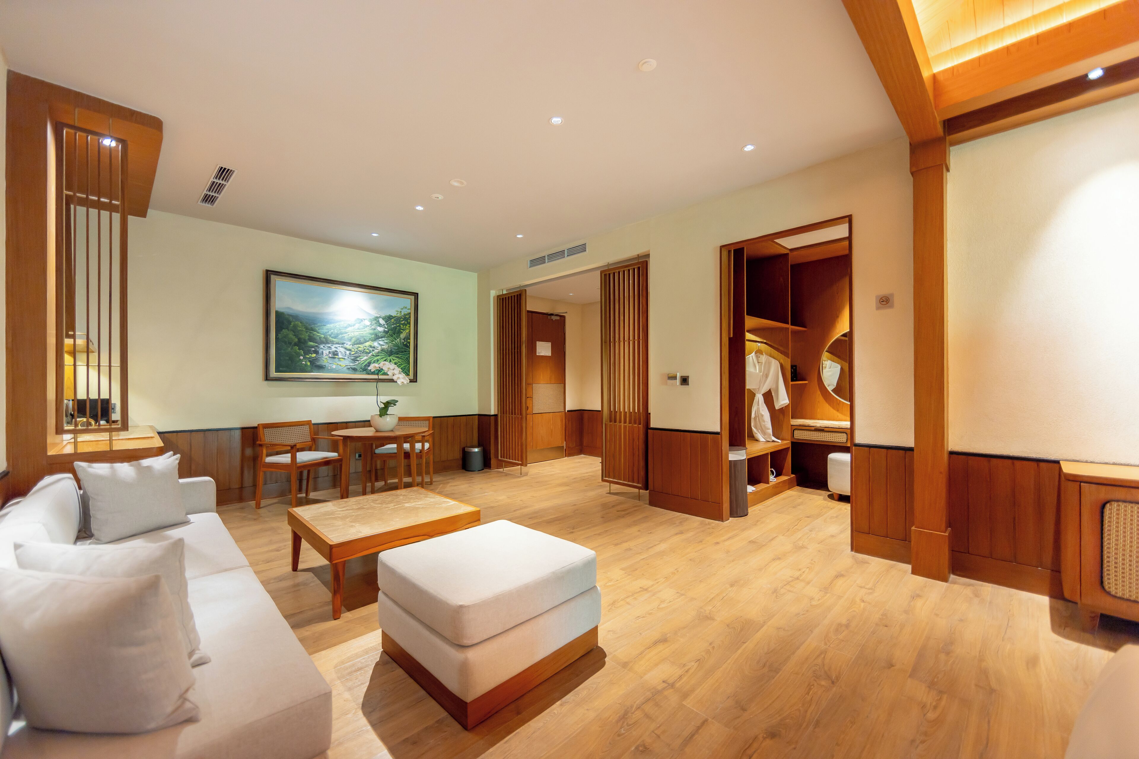 Quarto de hotel moderno com piso de madeira, sofá, mesa de jantar e closet espaçoso.