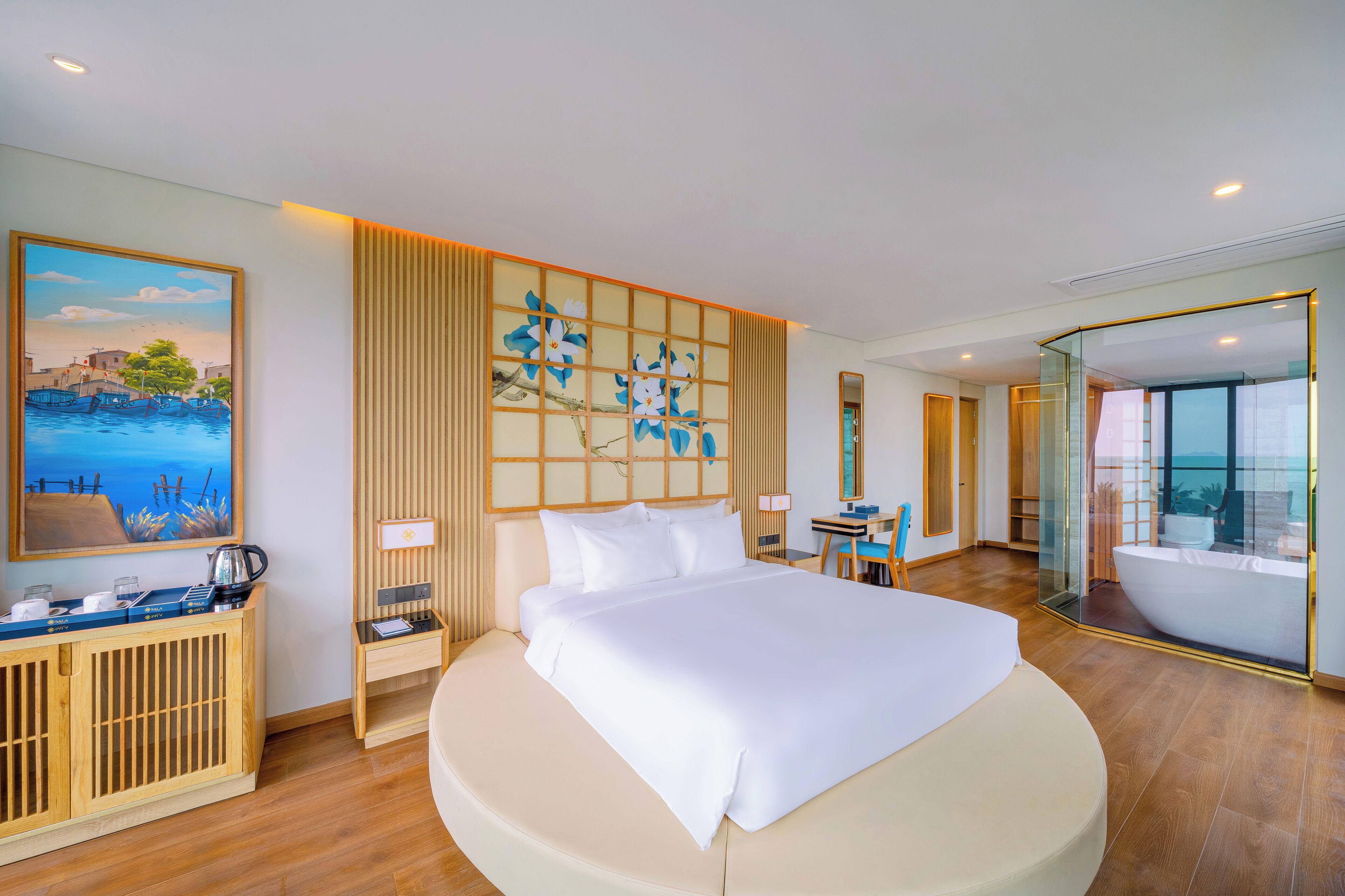 Quarto de hotel moderno com uma cama grande, uma mesa consola de madeira, uma escrivaninha, uma cadeira, um janelão e uma banheira.