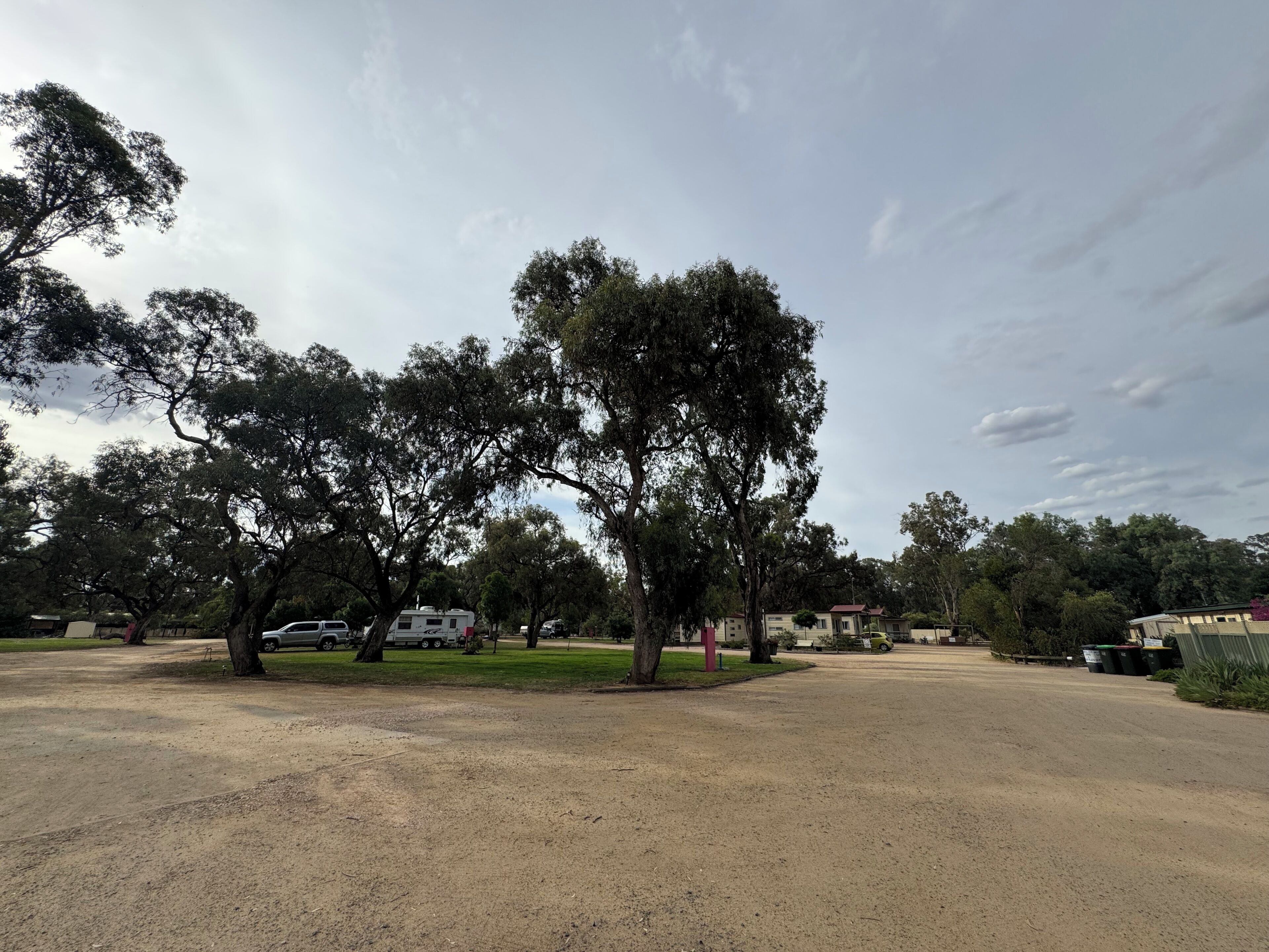 Um camping com veículos recreativos, árvores e uma estrada de terra.