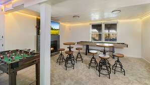 Quarto com mesa de pebolim, lareira e área de bar com banquetas.