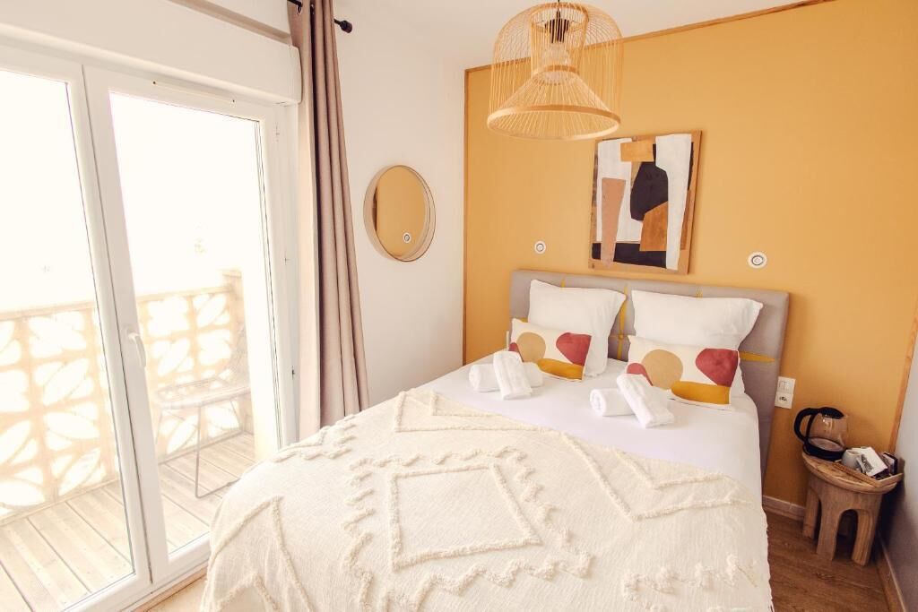 Quarto com cama, mesa de cabeceira, cadeira, janela e varanda.