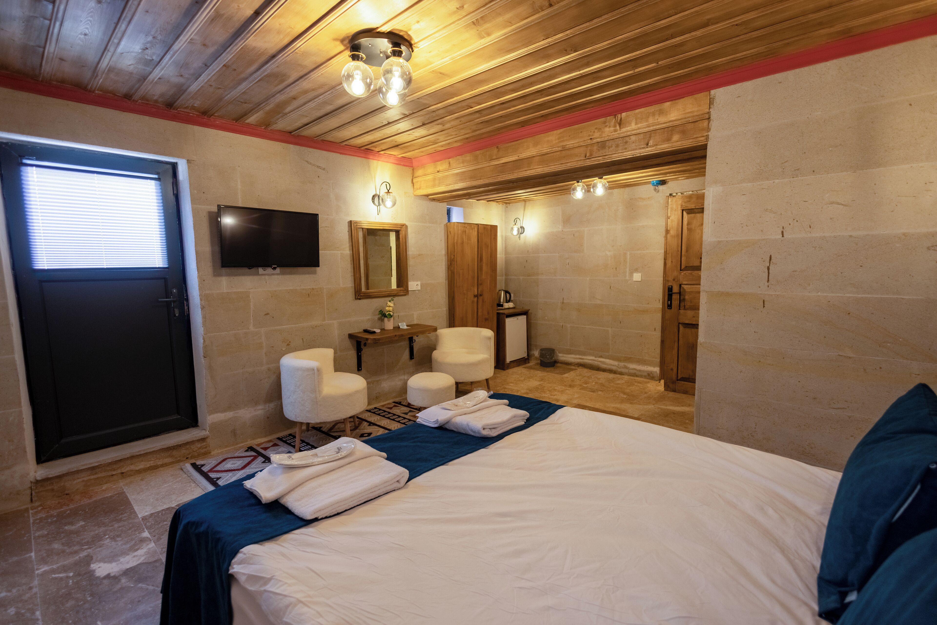 Quarto com uma cama grande, duas cadeiras, uma TV e teto de madeira.