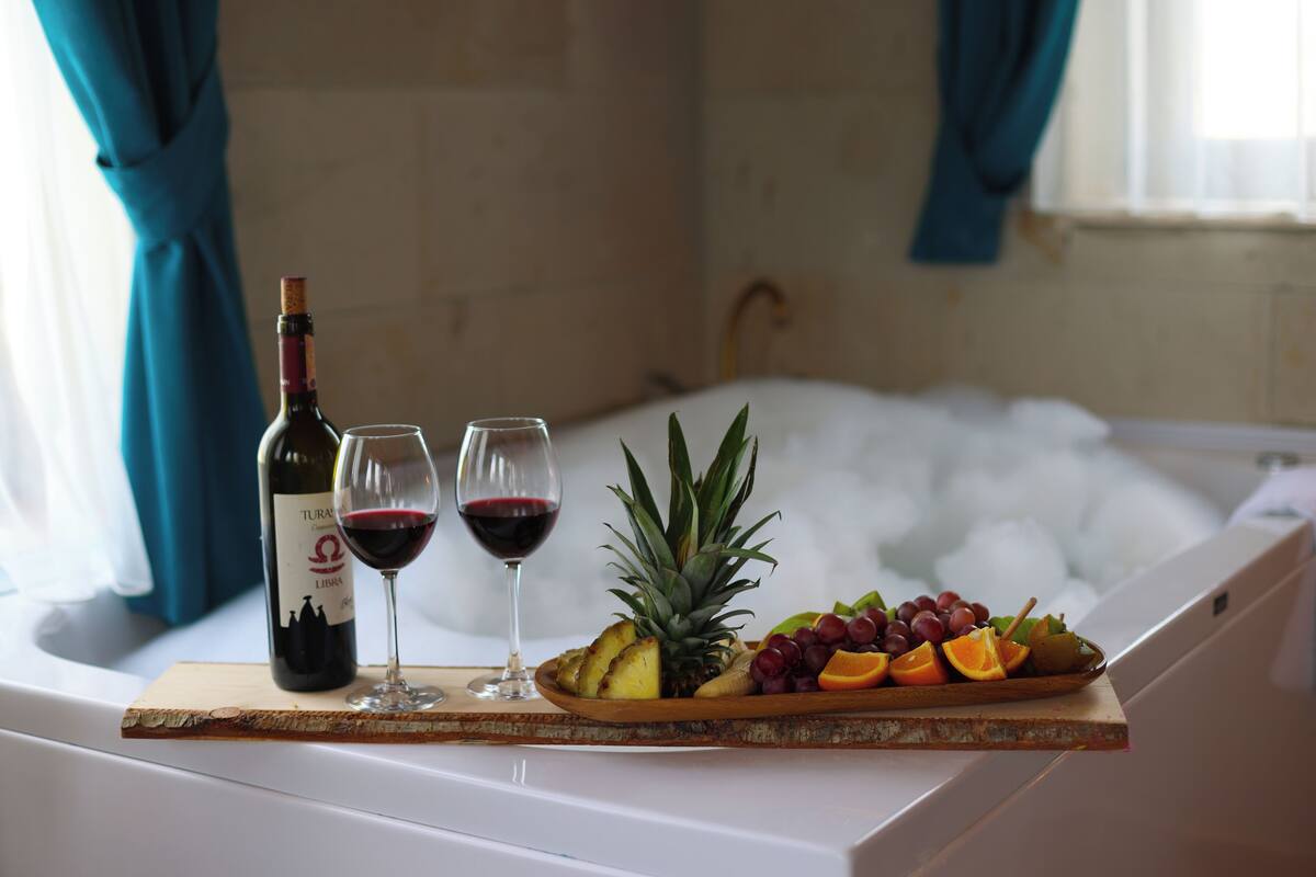 Uma banheira com uma bandeja de frutas e dois copos de vinho tinto.