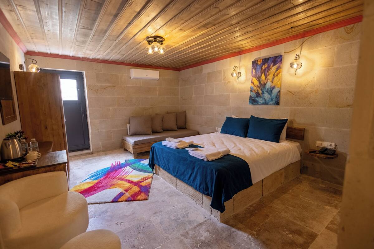 Quarto com cama, um banquinho, um tapete colorido e teto de madeira.