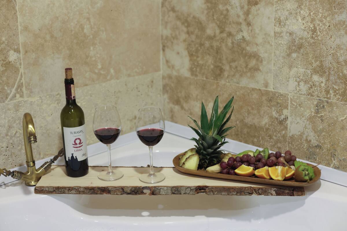 Uma garrafa de vinho, duas taças de vinho tinto e um prato de frutas sobre uma bandeja de madeira.