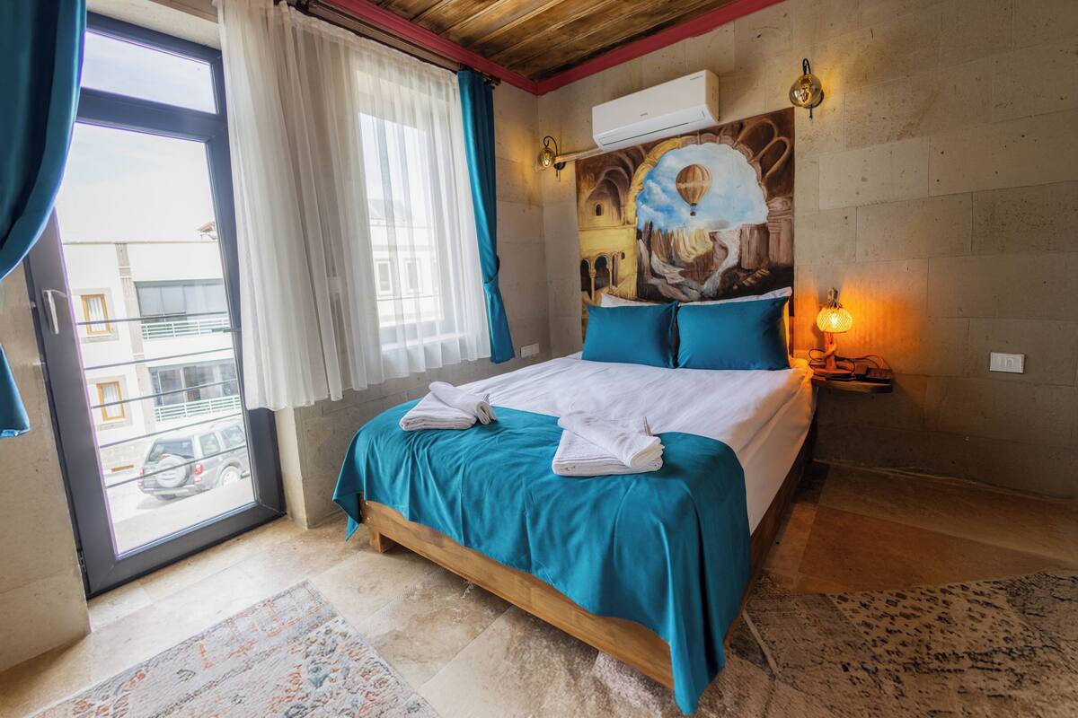 Quarto com cama, janela com cortinas, ar-condicionado fixado na parede e um quadro.