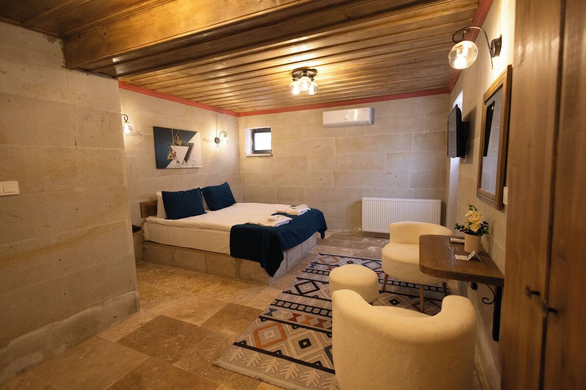 Quarto com cama, uma cadeira, mesa pequena, quadro e luminária no teto.