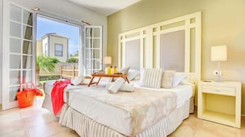 Quarto com cama grande, mesa de cabeceira, criadeira e janela com vista para o exterior.