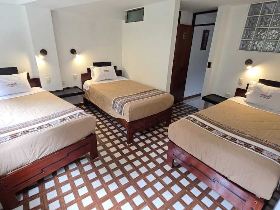 Quarto de hotel com três camas, piso quadriculado e porta que dá para outro cômodo.