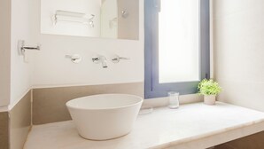 Uma casa de banho moderna com uma grande pia branca, um espelho, um porta-toalhas e uma pequena planta em vaso.