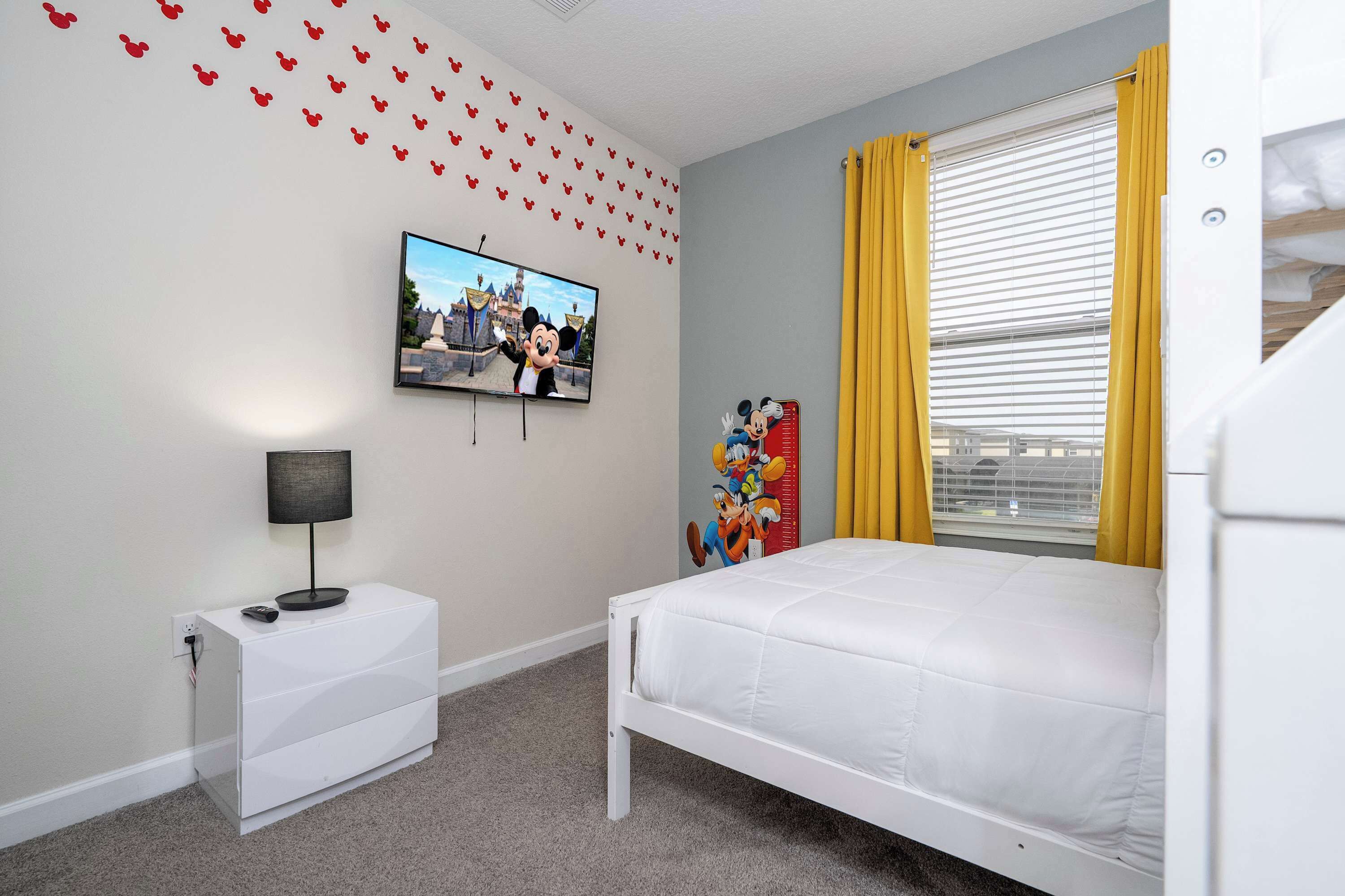 Quarto com cama, televisão, mesa de cabeceira e decoração com o Mickey Mouse.