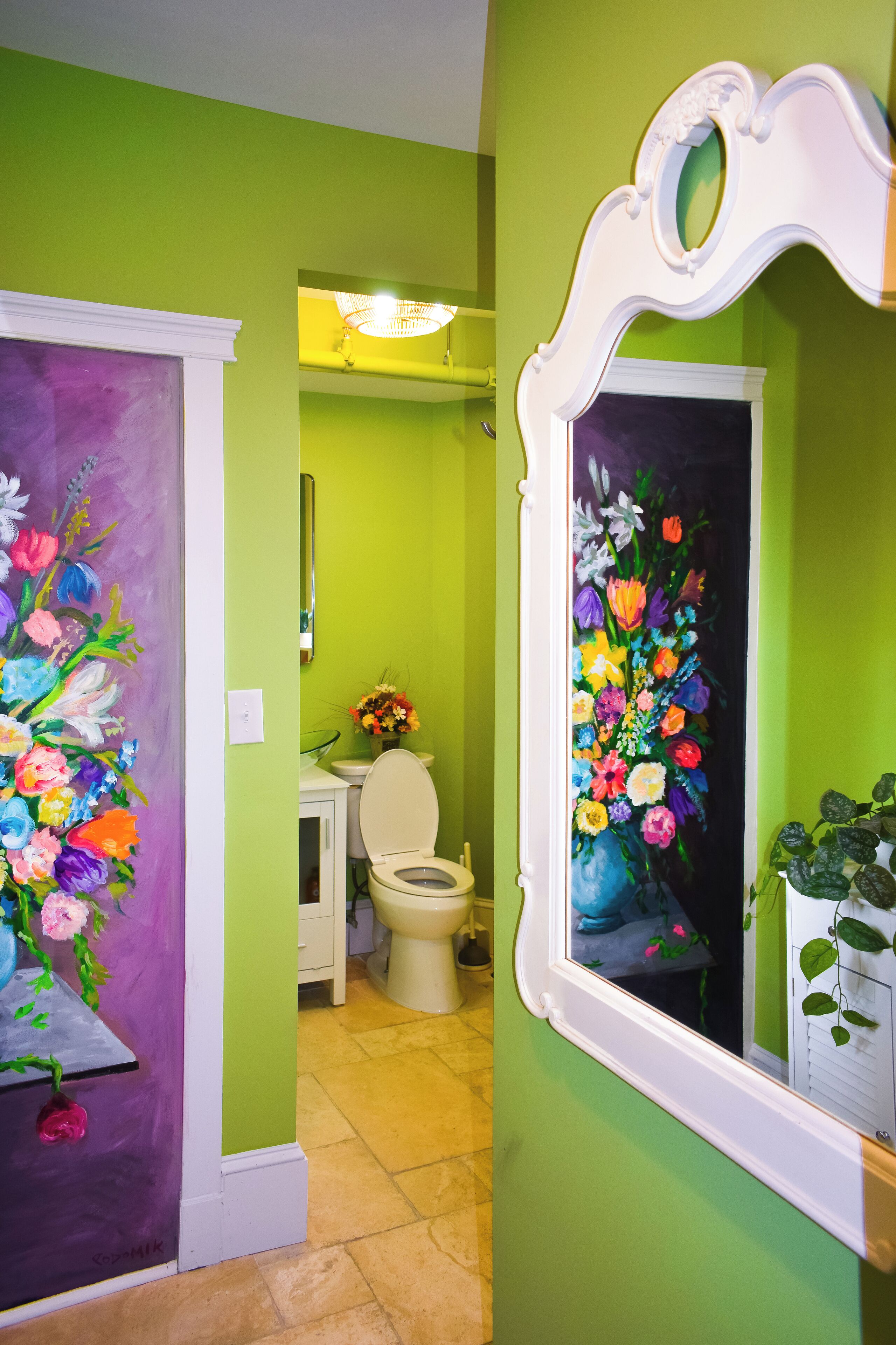 Casa de banho com paredes verdes, sanita branca e espelho com motivos florais.
