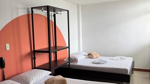 Quarto de hotel com duas camas, uma estante de metal preta, um telefone e uma parede em destaque vermelha.