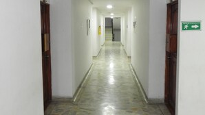 Um corredor com paredes brancas, chão de azulejos e um sinal de saída de emergência verde.