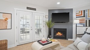 Uma sala de estar com lareira, uma TV de tela plana montada acima e uma placa com a inscrição 'Welcome to the Back Porch'.