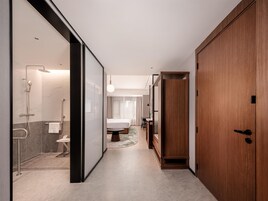 Corredor moderno de hotel com área de chuveiro, uma cama e um armário de madeira.