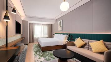 Quarto de hotel moderno com uma cama grande, um sofá, uma mesa de centro, uma escrivaninha e uma televisão.