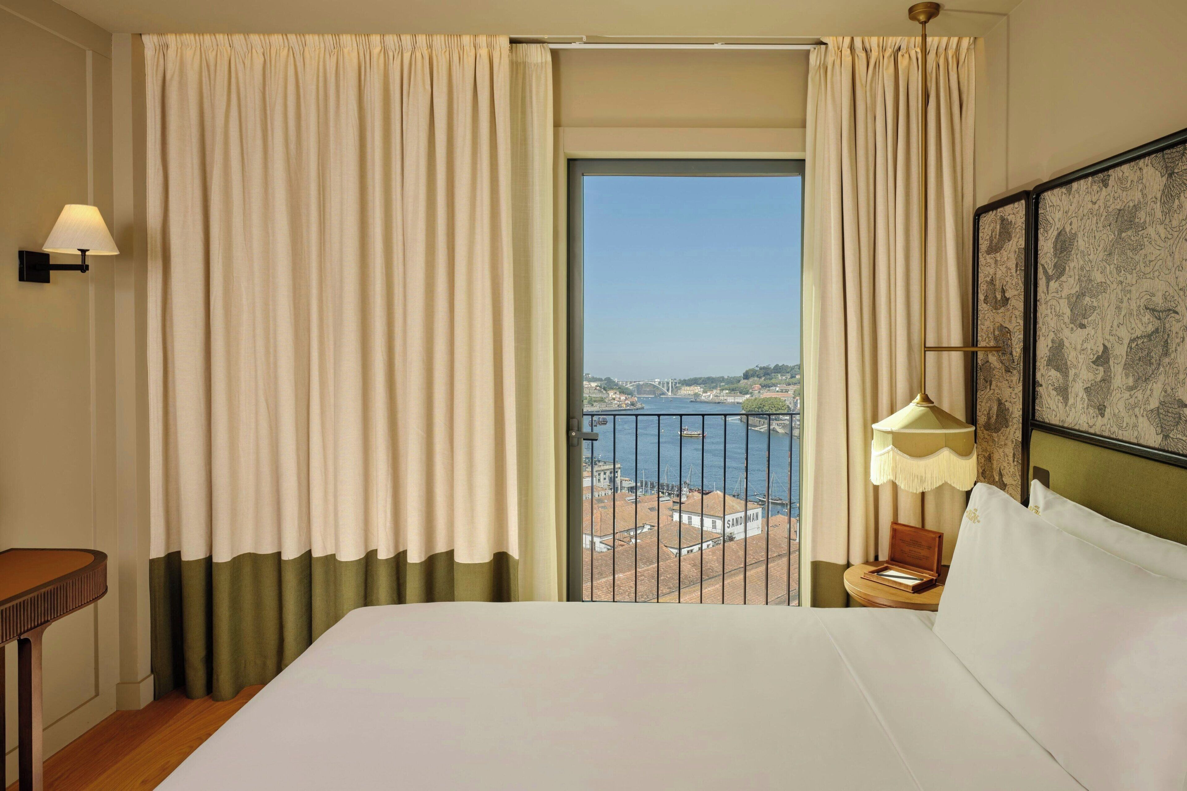 Quarto de hotel com uma cama grande, vista para um porto de iates e uma mesa de cabeceira com abajur.