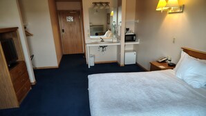 Quarto de hotel com uma cama grande, uma escrivaninha com espelho, micro-ondas e telefone num criado-mudo.