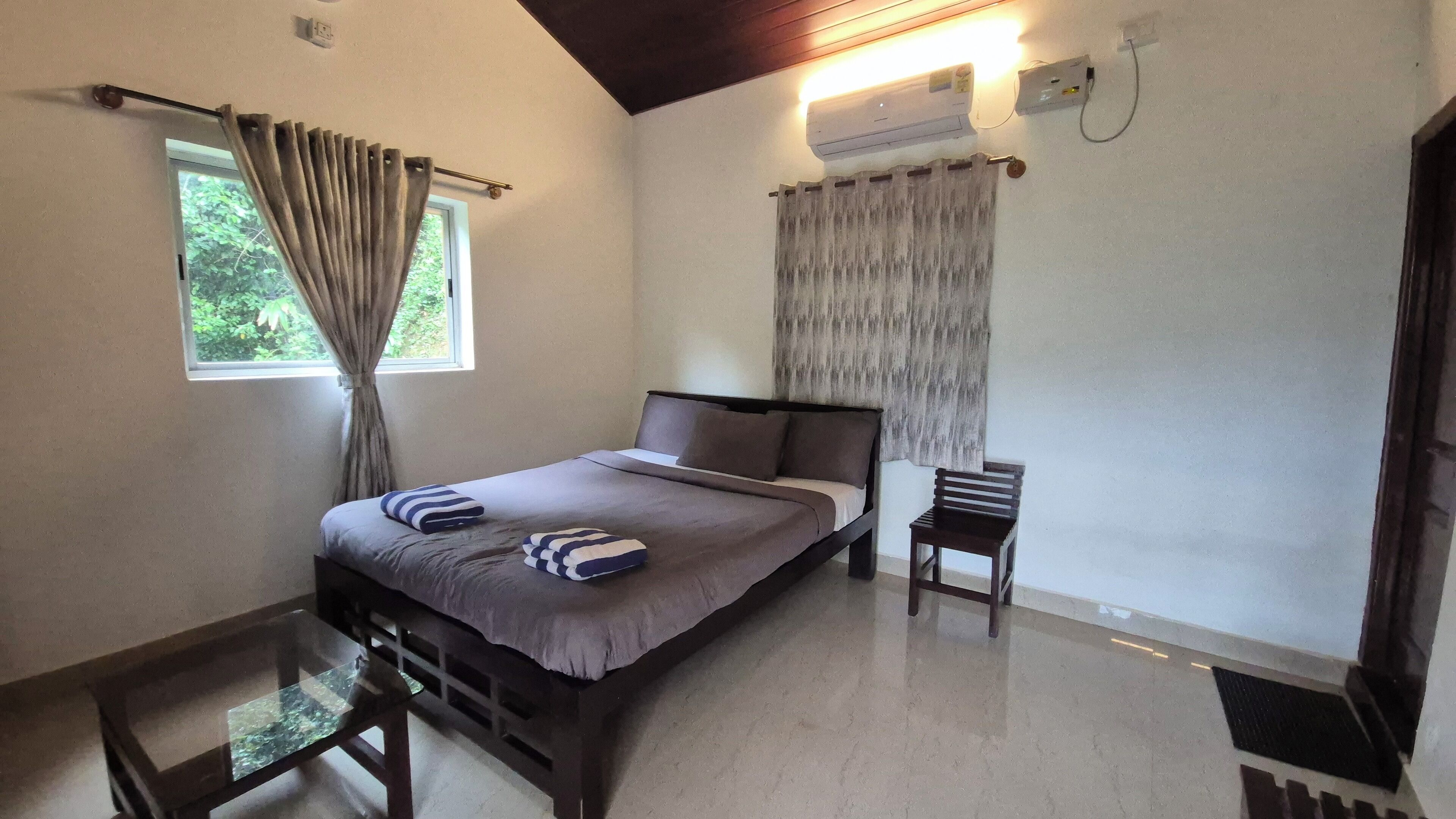 Quarto com cama, cadeira, mesa e janela com cortinas.