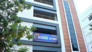 Um edifício de vários andares com uma placa de destaque que diz "Home Stay", uma escadaria e duas scooters estacionadas.