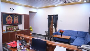 Quarto com escrivaninha de madeira, sofá azul, relógio na parede e ventilador de teto.