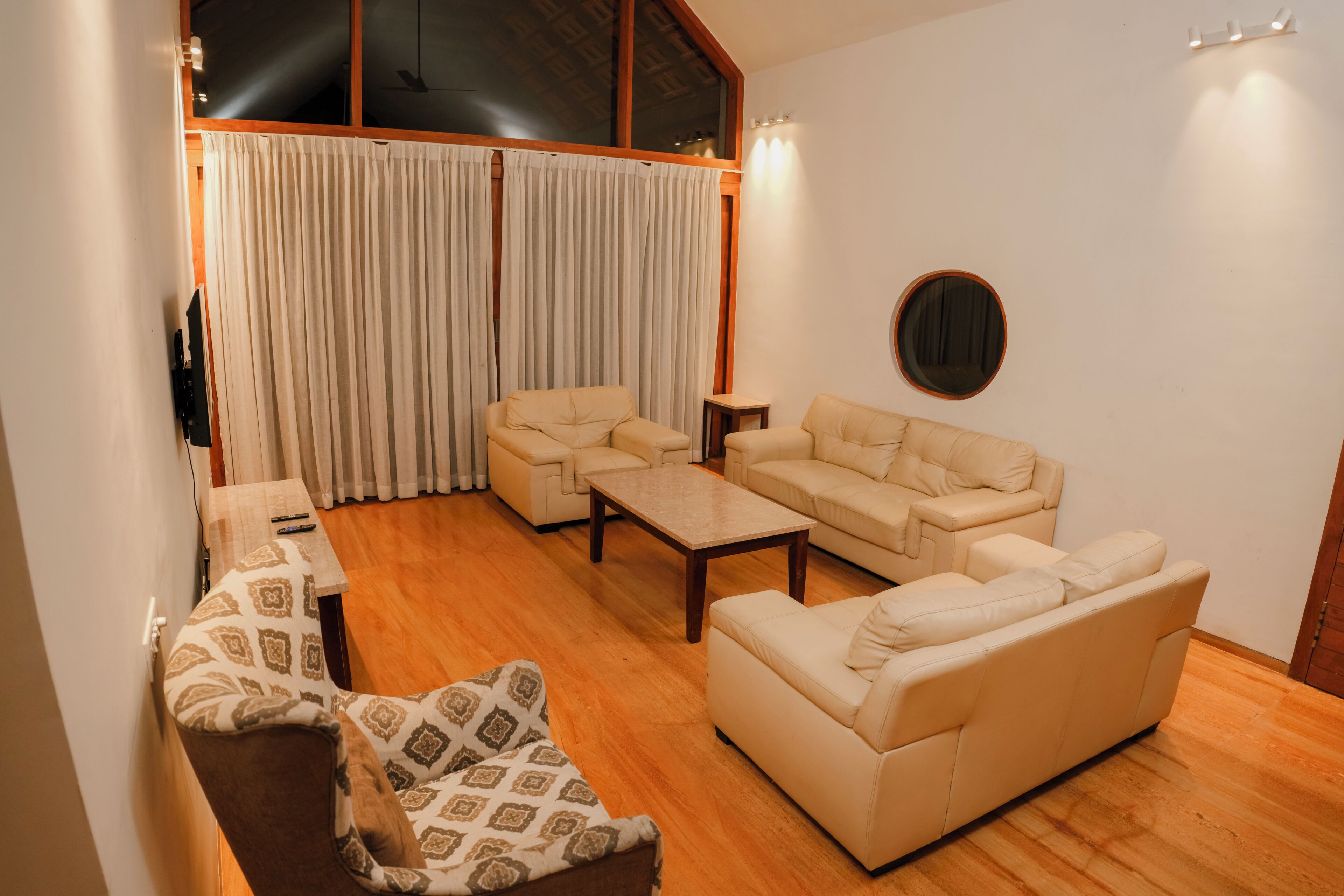 Sala de estar com sofá, poltrona e mesa de centro, uma pequena mesa lateral e um espelho redondo na parede.