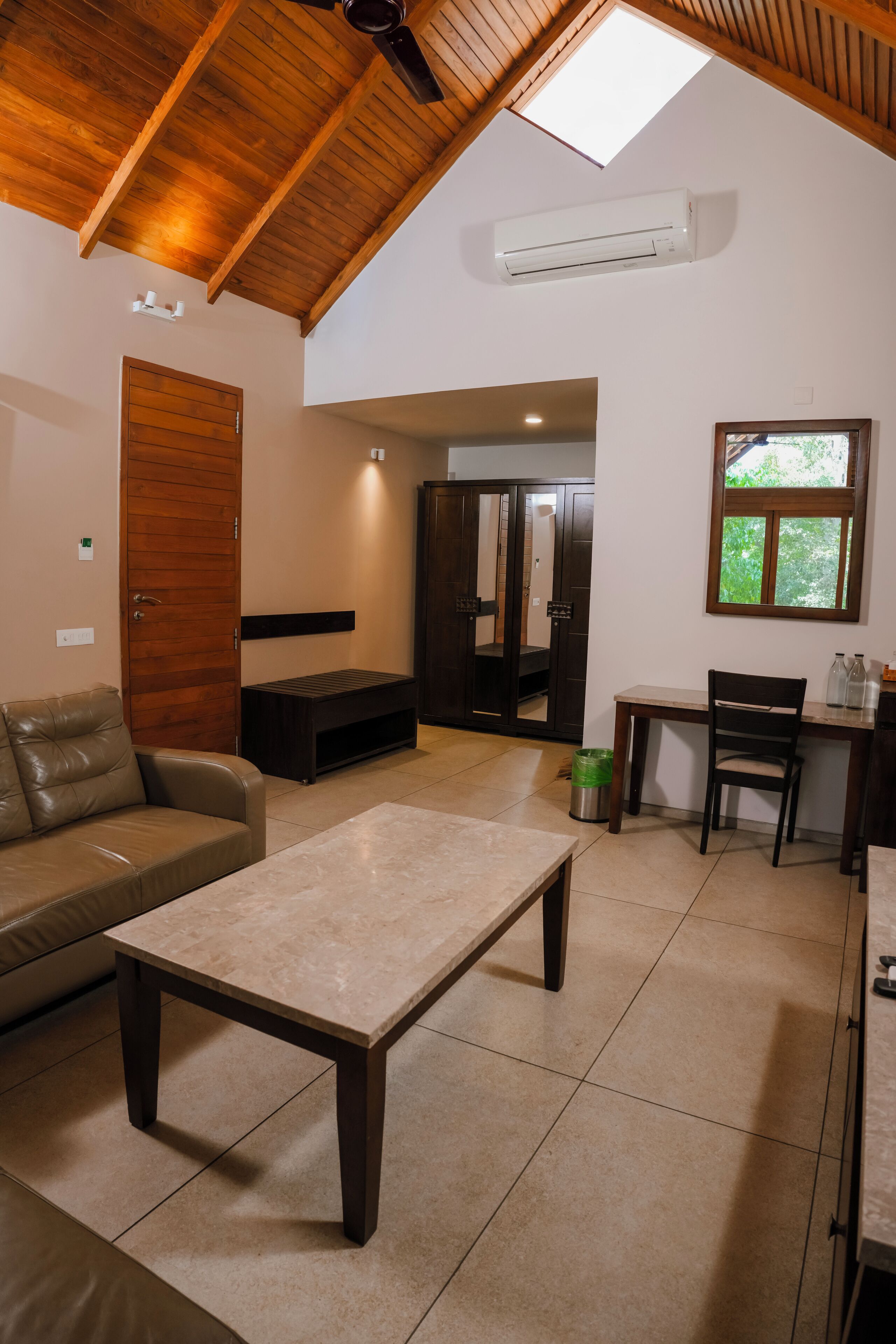 Uma sala de estar moderna com teto de madeira, um sofá bege, uma mesa de centro, uma TV e uma janela com vista para o verde.