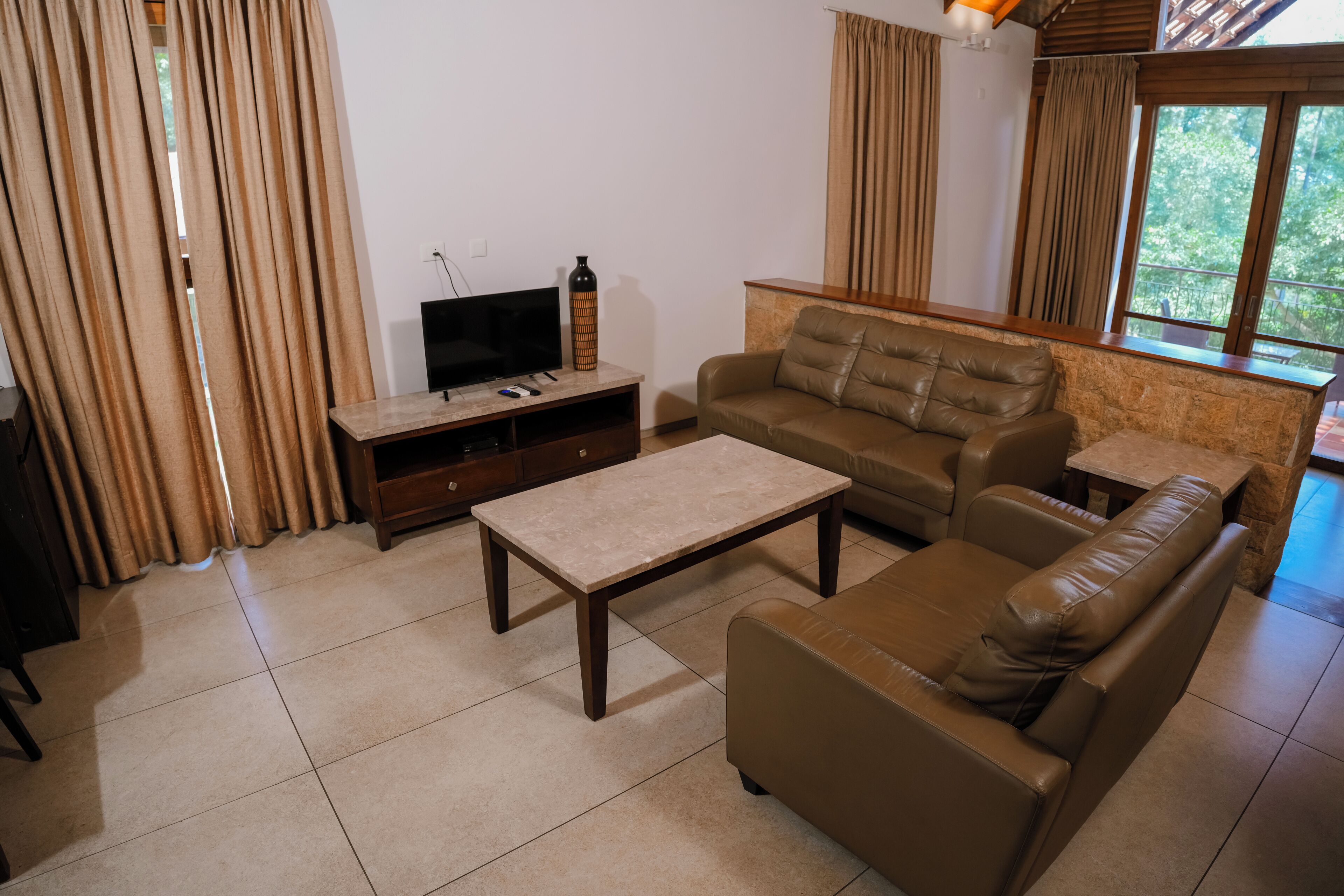 Uma sala de estar com sofá de couro, mesa de centro, rack para TV e cortinas.
