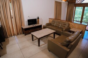 Uma sala de estar com sofá de couro, mesa de centro, rack para TV e cortinas.