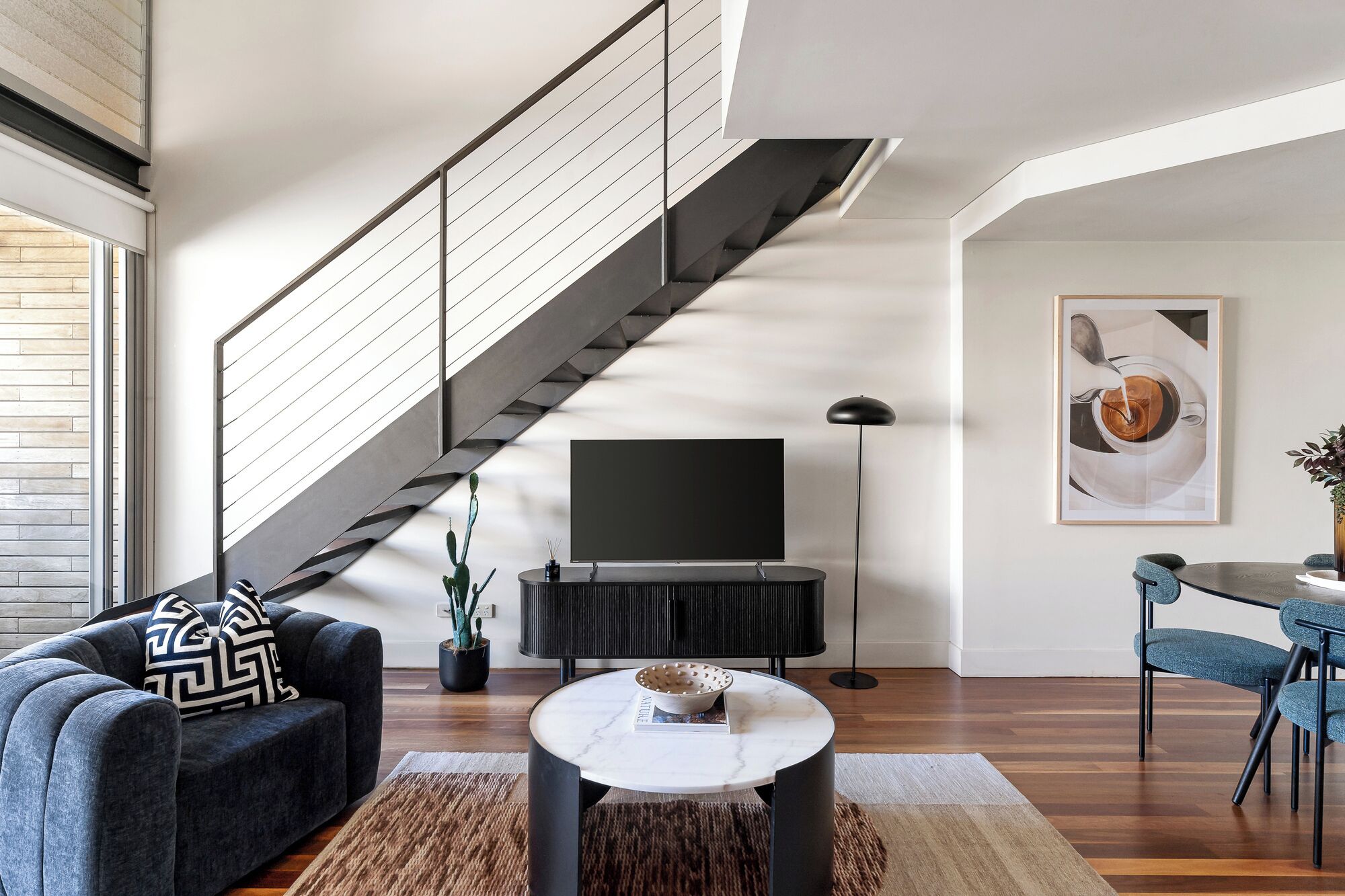 Uma sala de estar moderna com escada, televisão de tela plana, mesa de centro e área de jantar.