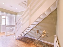 Interior moderno com piso de madeira, escada branca e porta de vidro que dá para o exterior.
