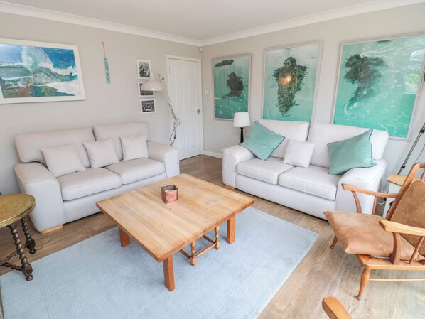 Uma sala de estar moderna com dois sofás brancos, uma mesa de centro de madeira e uma poltrona de madeira.