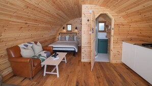 Uma cabana acolhedora com decoração em madeira, uma cama, um sofá e uma cozinha compacta.