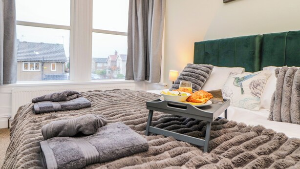 Quarto de hotel com uma cama grande, uma mesa de cabeceira com itens de café da manhã, vista para o exterior e cabeceira verde.