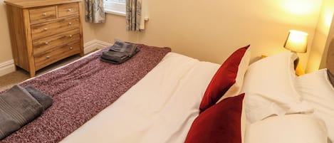 Um quarto com uma cama, cômoda de madeira, janela com cortinas estampadas e abajur.