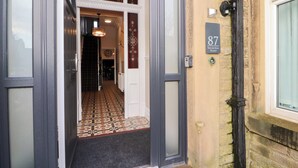 Entrada de hotel com piso de azulejos, porta com pain éis de vidro e um poste de luz.