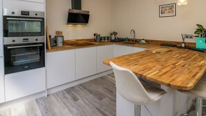 Uma cozinha moderna com armários brancos, bancada de madeira, eletrodomésticos de aço inoxidável e iluminação pendente.