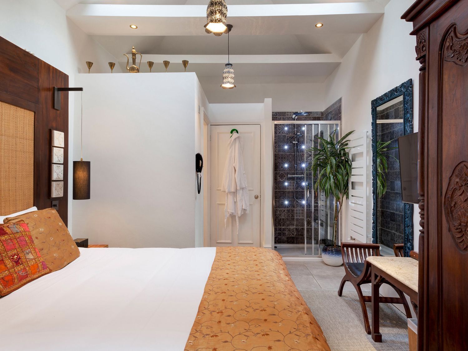 Quarto com cama grande, escrivaninha, cadeira, telefone e área de chuveiro.