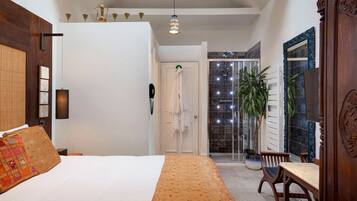 Quarto com cama grande, escrivaninha, cadeira, telefone e área de chuveiro.