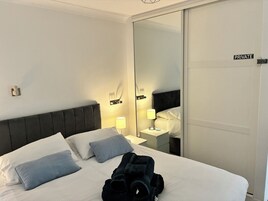 Quarto de hotel com cama, duas almofadas, mesa de cabeceira com abajur, espelho e placa na porta com a palavra 'PRIVATE'.